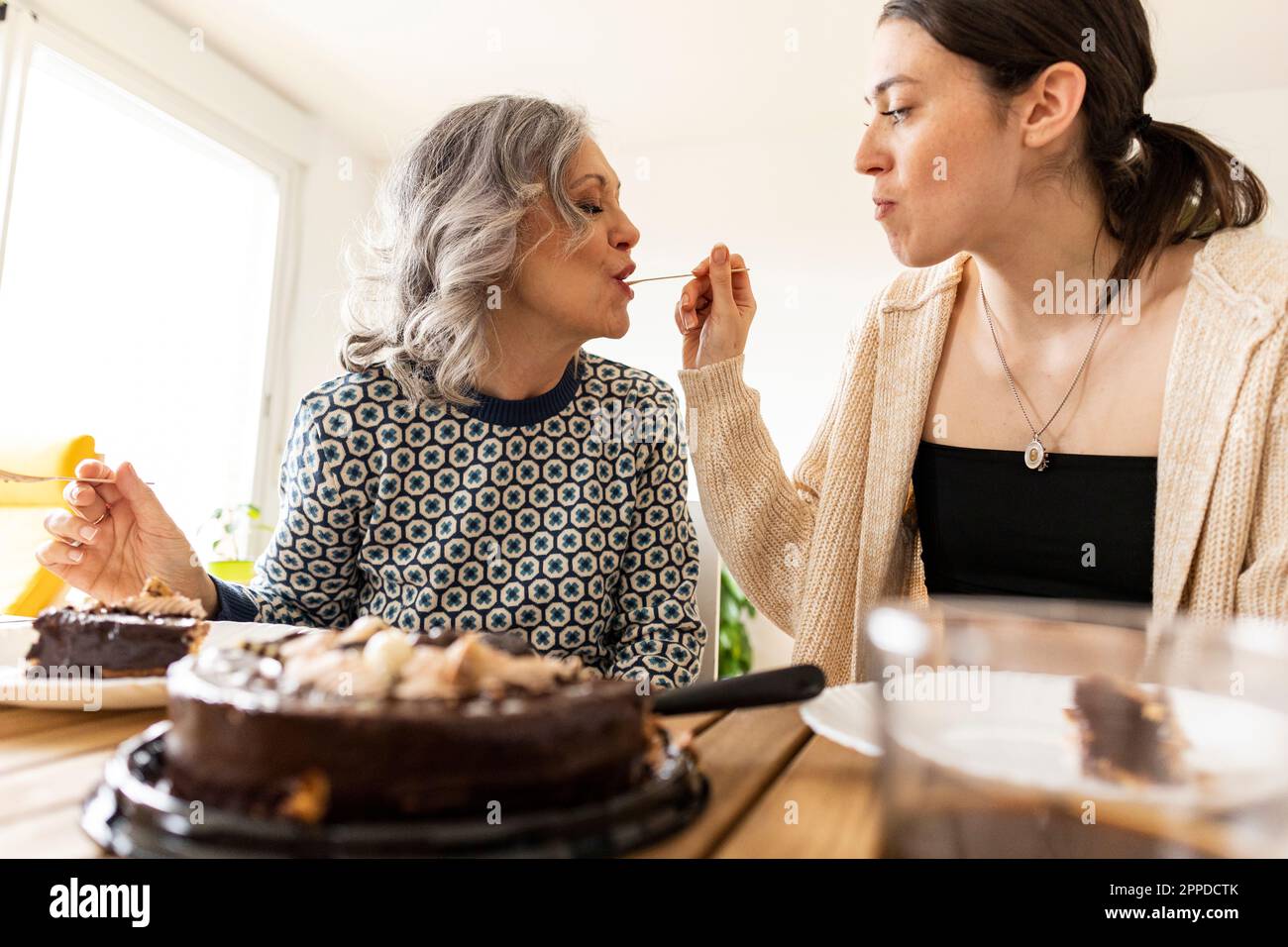 Daughter feeding cake and taking care of mother at home Stock Photo - Alamy