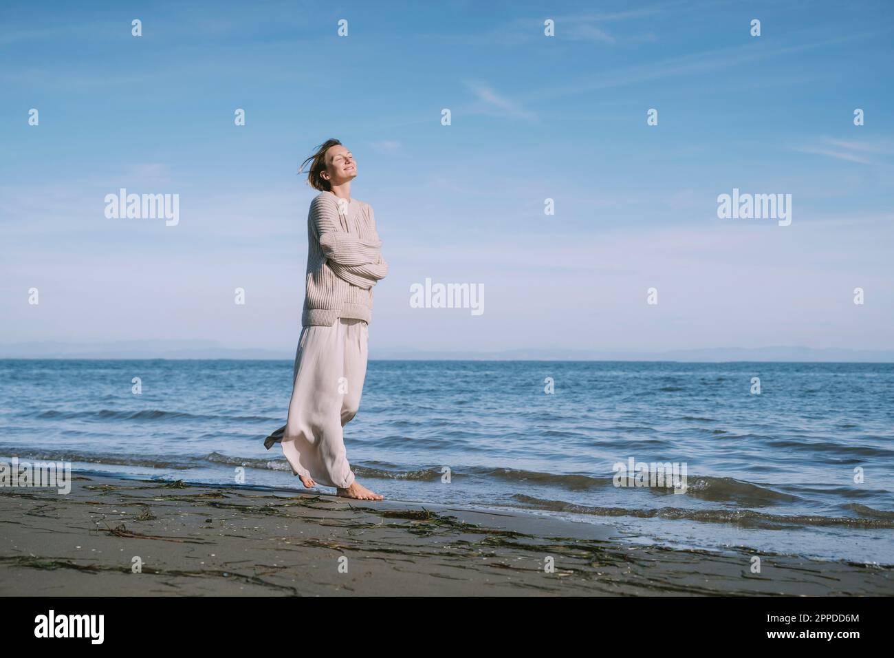 Solitude woman with arms crossed walking on shore at beach Stock Photo ...