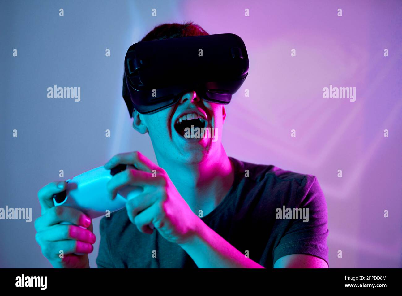 Excited young playing video game through VR glasses in front of wall ...