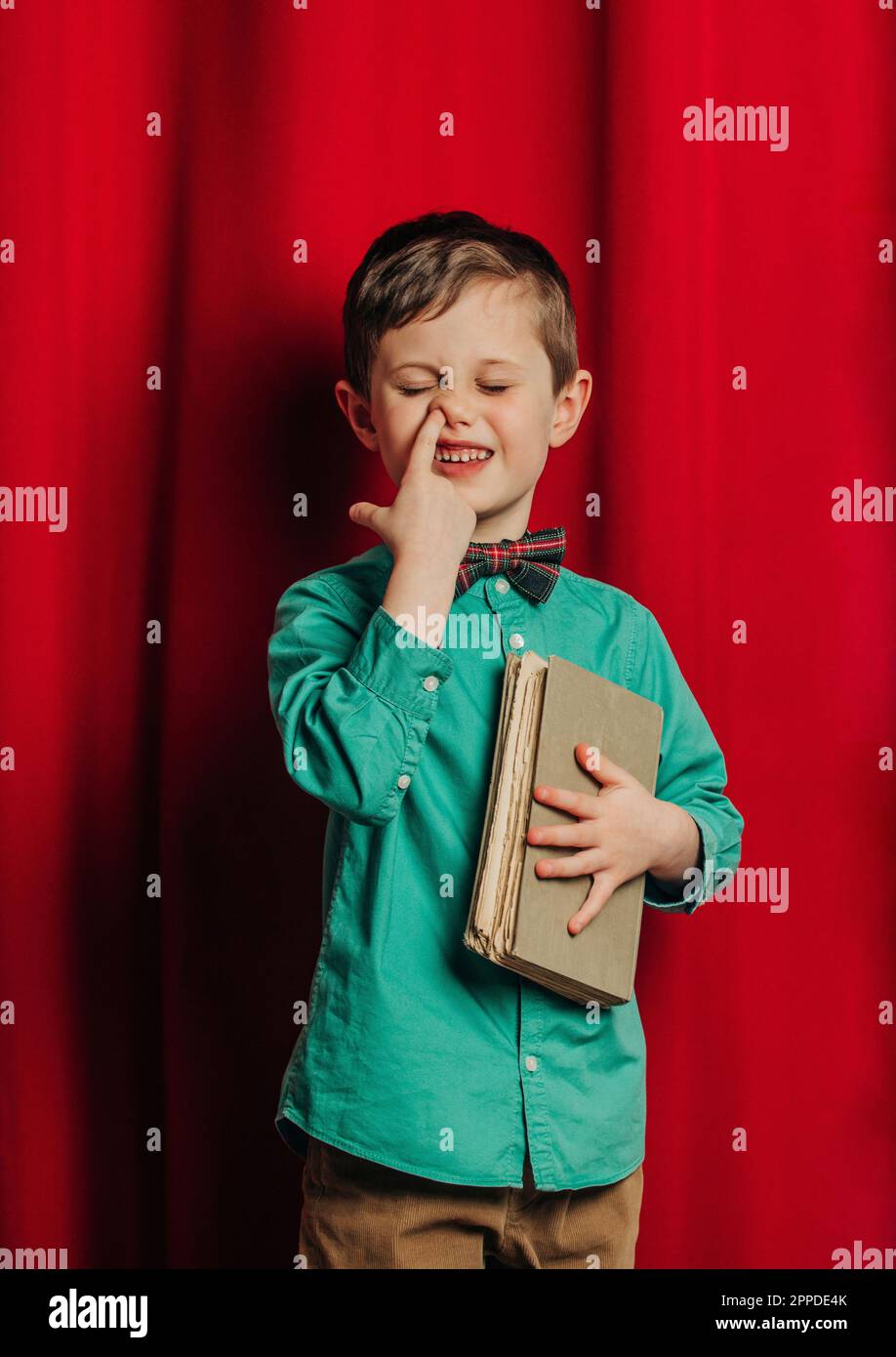 Boy wearing bow tie and green shirt with book picking nose in front of ...