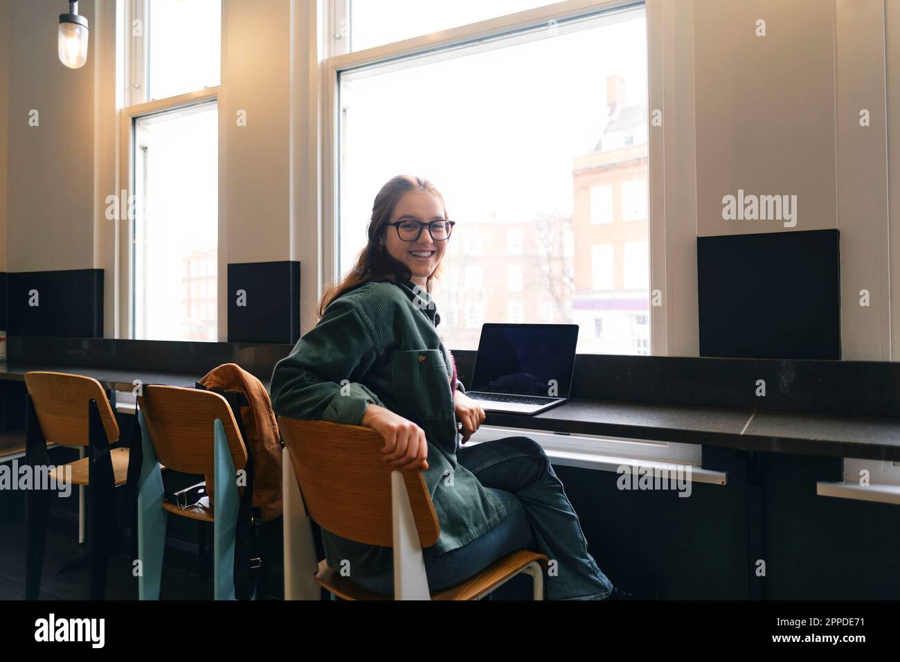 Smiling young freelancer sitting on chair by window at cafe Stock Photo ...