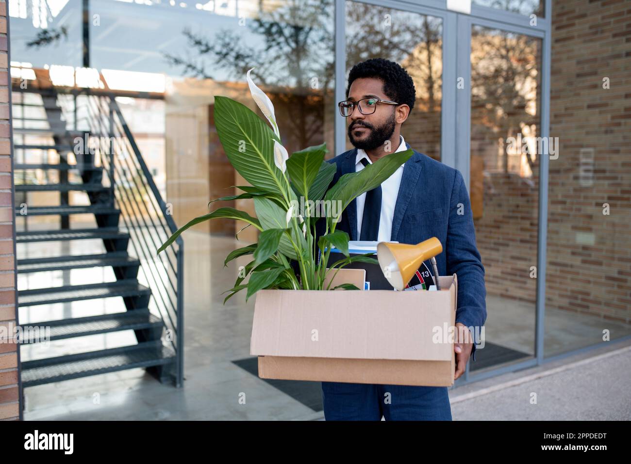 Thoughtful businessman carrying cardboard box leaving office building ...
