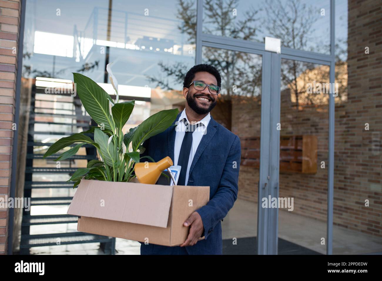 Smiling businessman leaving office building carrying cardboard box ...