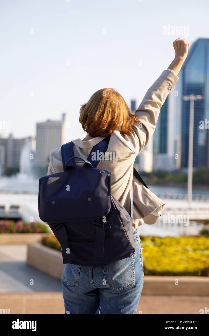 Businesswoman wearing backpack cheering with hand raised Stock Photo ...