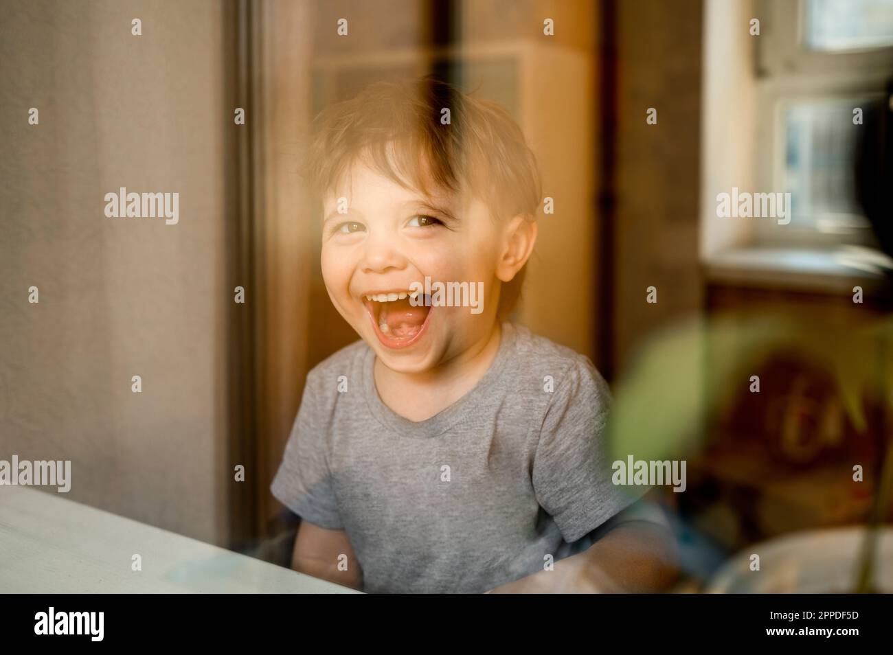 Cheerful cute boy seen through glass window Stock Photo - Alamy