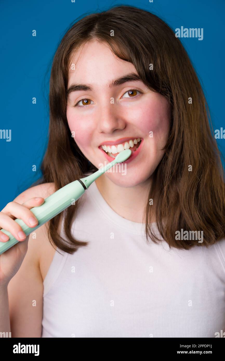 Happy Teenage Girl Holding Electric Toothbrush Seated | Blue Background ...