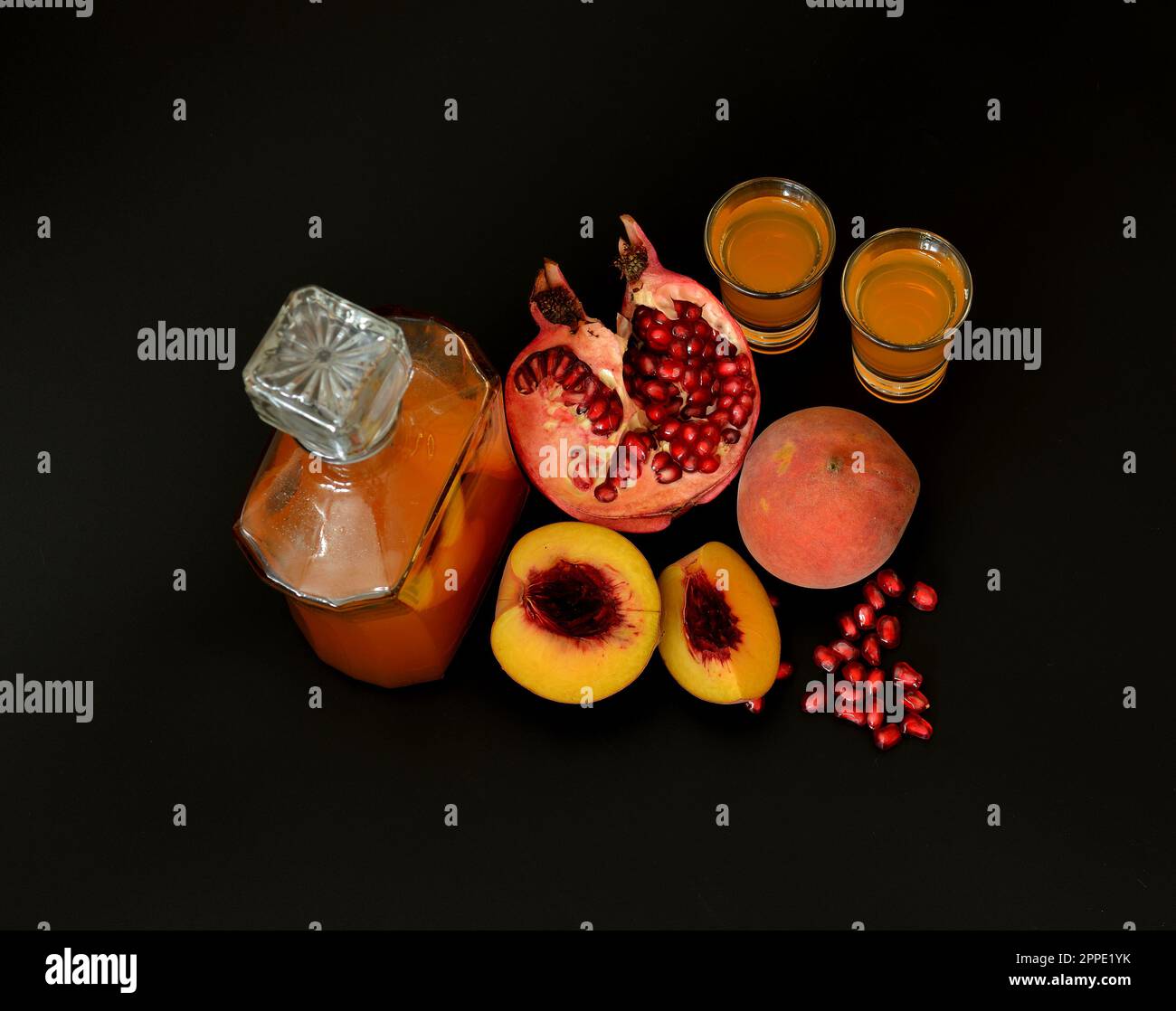 Homemade liqueur in a bottle and two glasses on a black background, next to pieces of a ripe ...