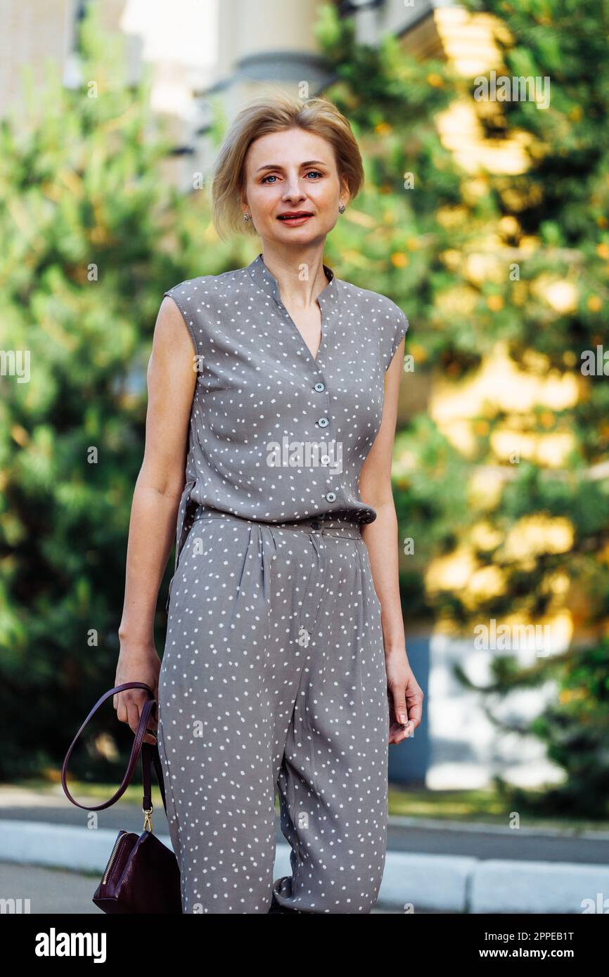 Portrait of stylish 40 years old woman walking outdoors among growing ...