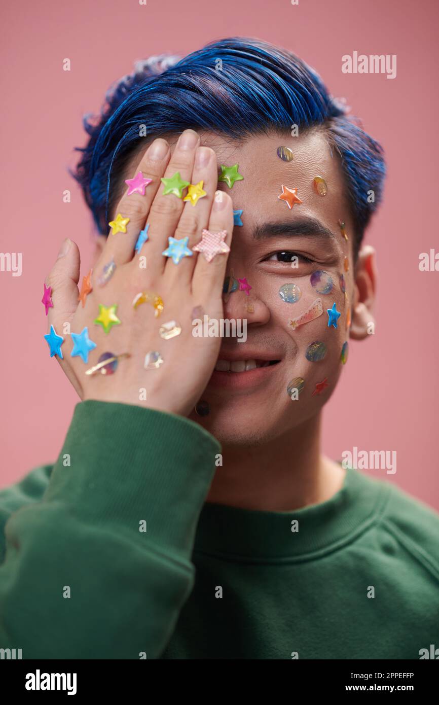 Creative smiling young man with bright stickers on face and hands ...