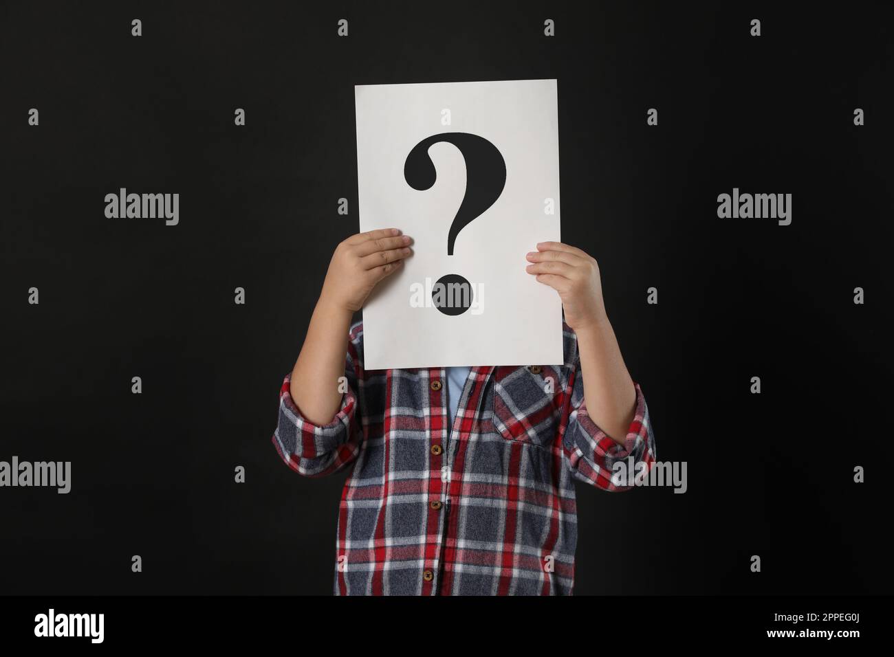 Child holding sheet of paper with question mark on black background ...