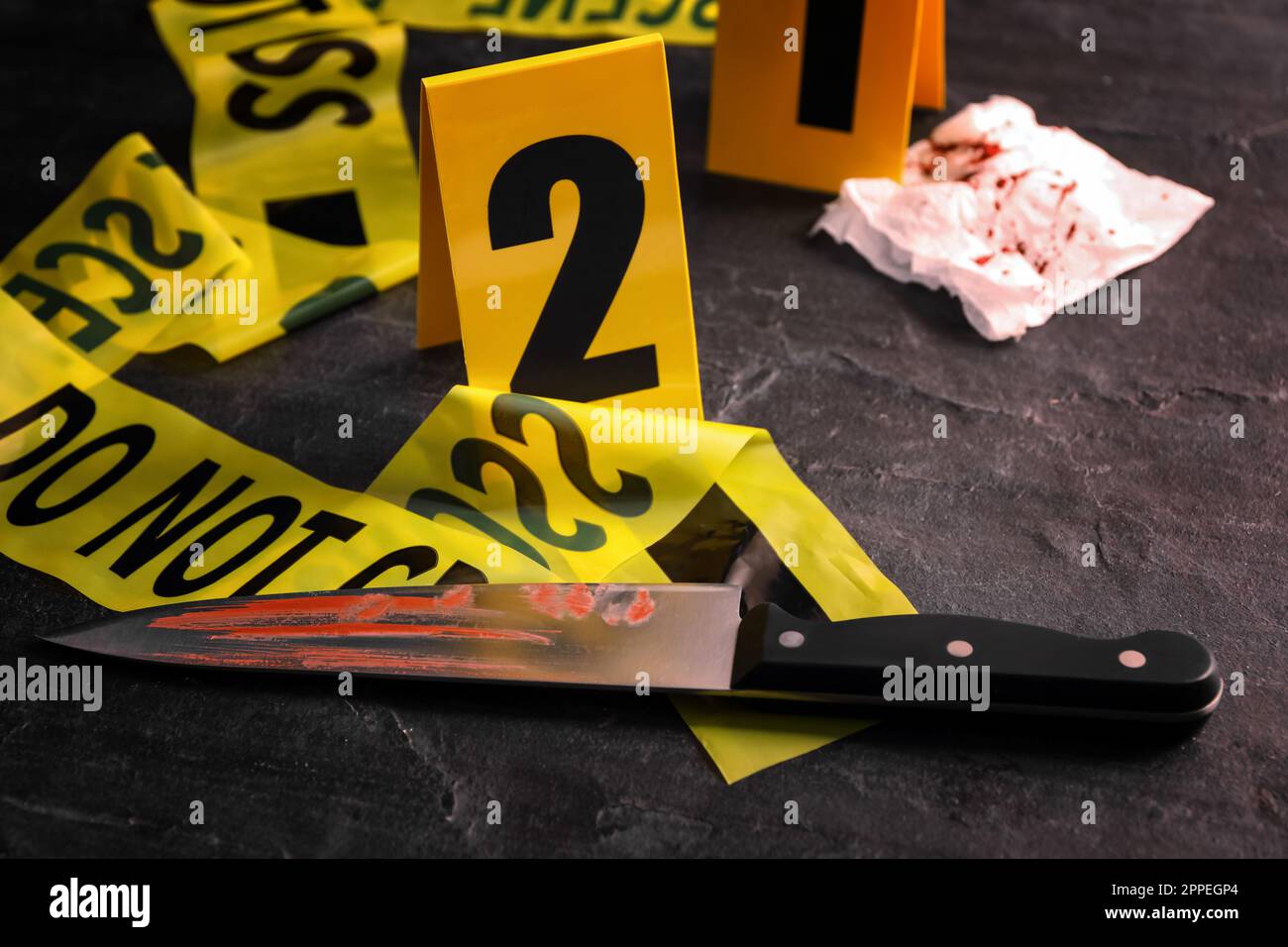 Bloody knife, yellow tape and evidence marker on black slate table ...