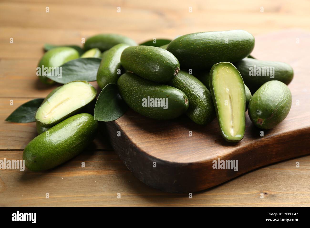 Fresh seedless avocados with green leaves on wooden table, closeup ...