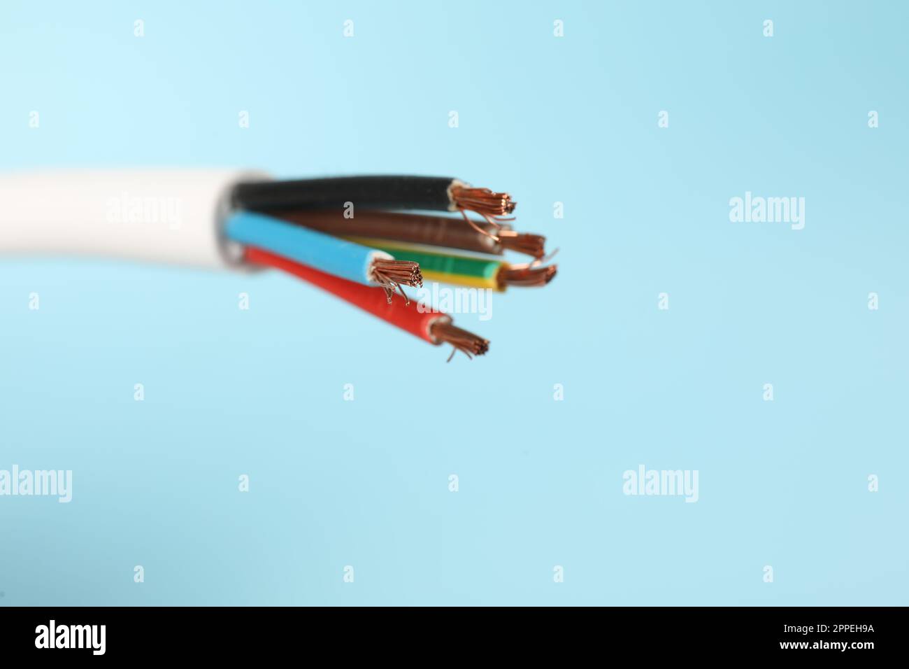 Cable with stripped electrical wires on light blue background, closeup ...