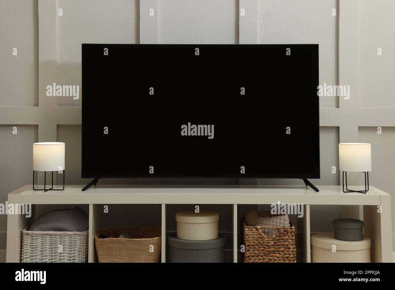 Modern TV and lamps on cabinet near white wall indoors. Interior design ...