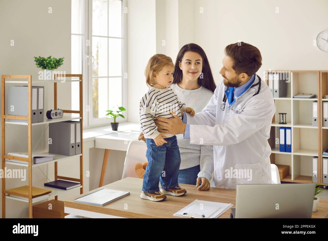 Caring, friendly doctor examines his little patient, smiling mother at ...