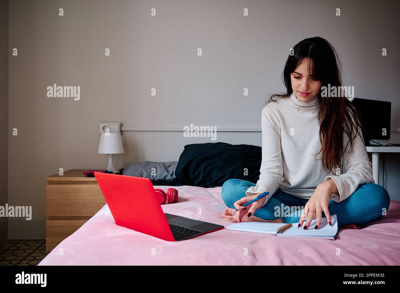 Woman taking notes while using a laptop sitting on the bed Stock Photo ...
