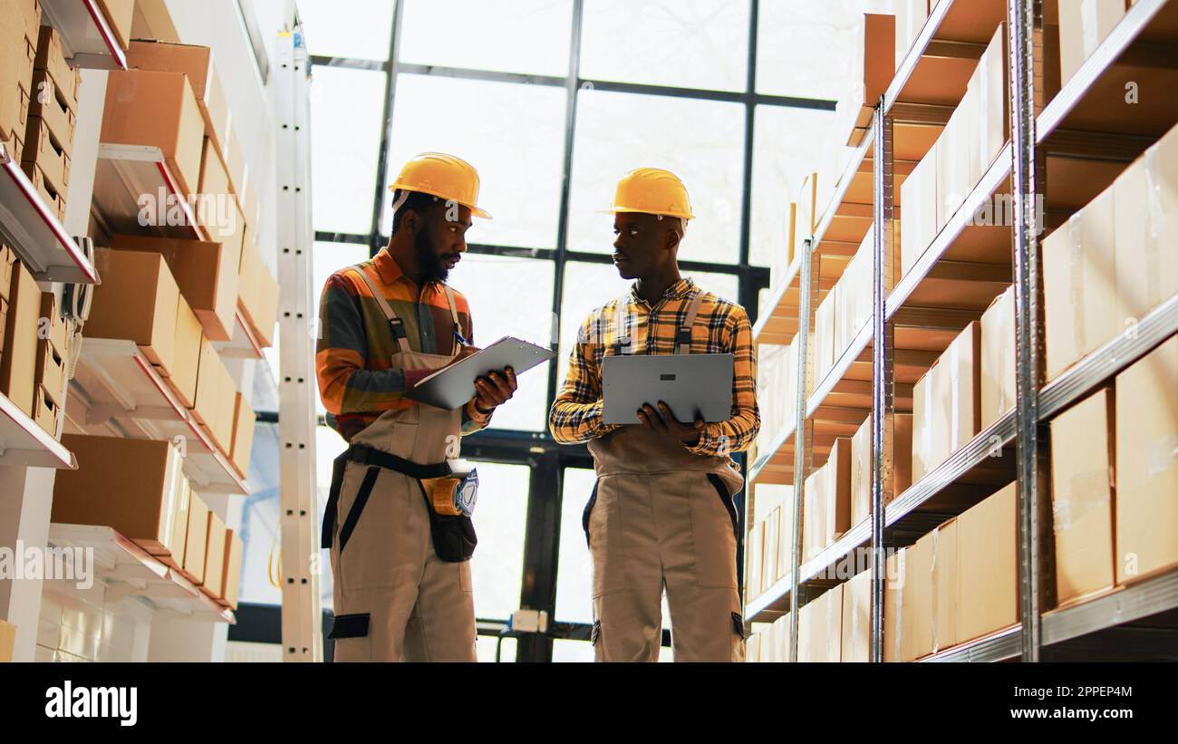 Two men working with laptop and clipboard lists to plan stock logistics ...