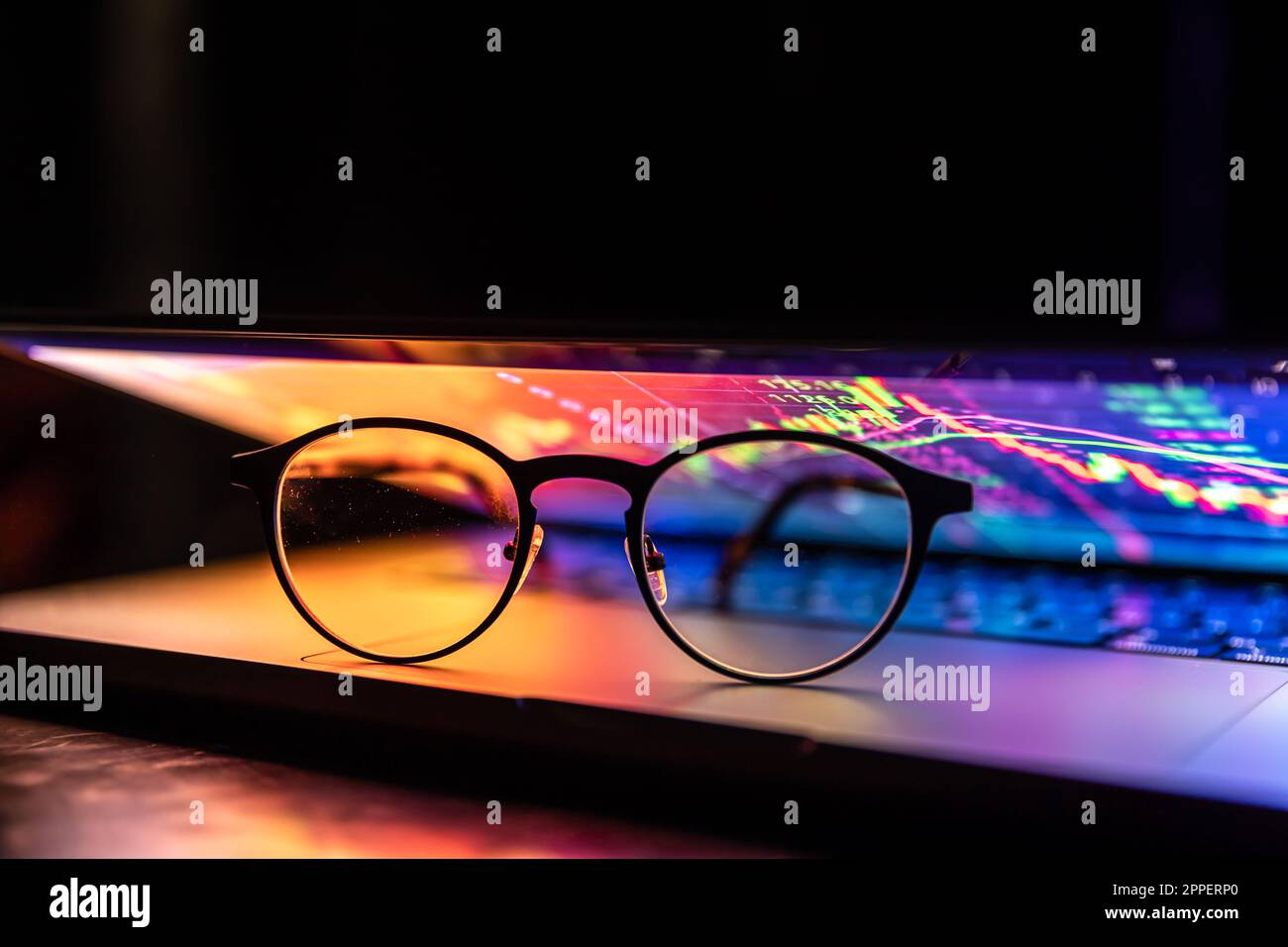A laptop half closed in the dark with colourful glow and glasses Stock ...