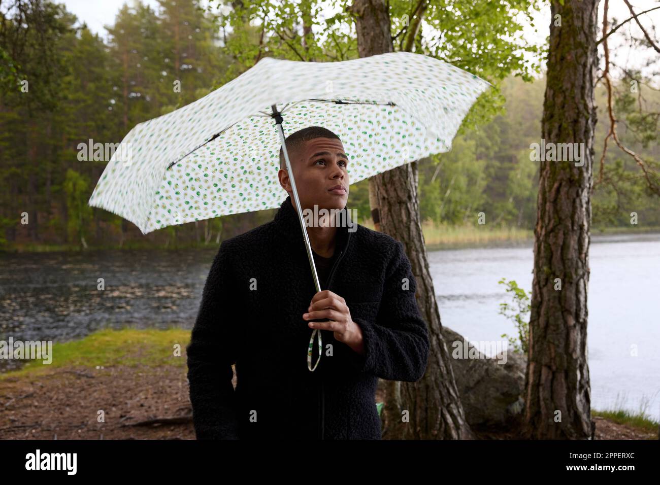 Young man holding umbrella at lake Stock Photo - Alamy
