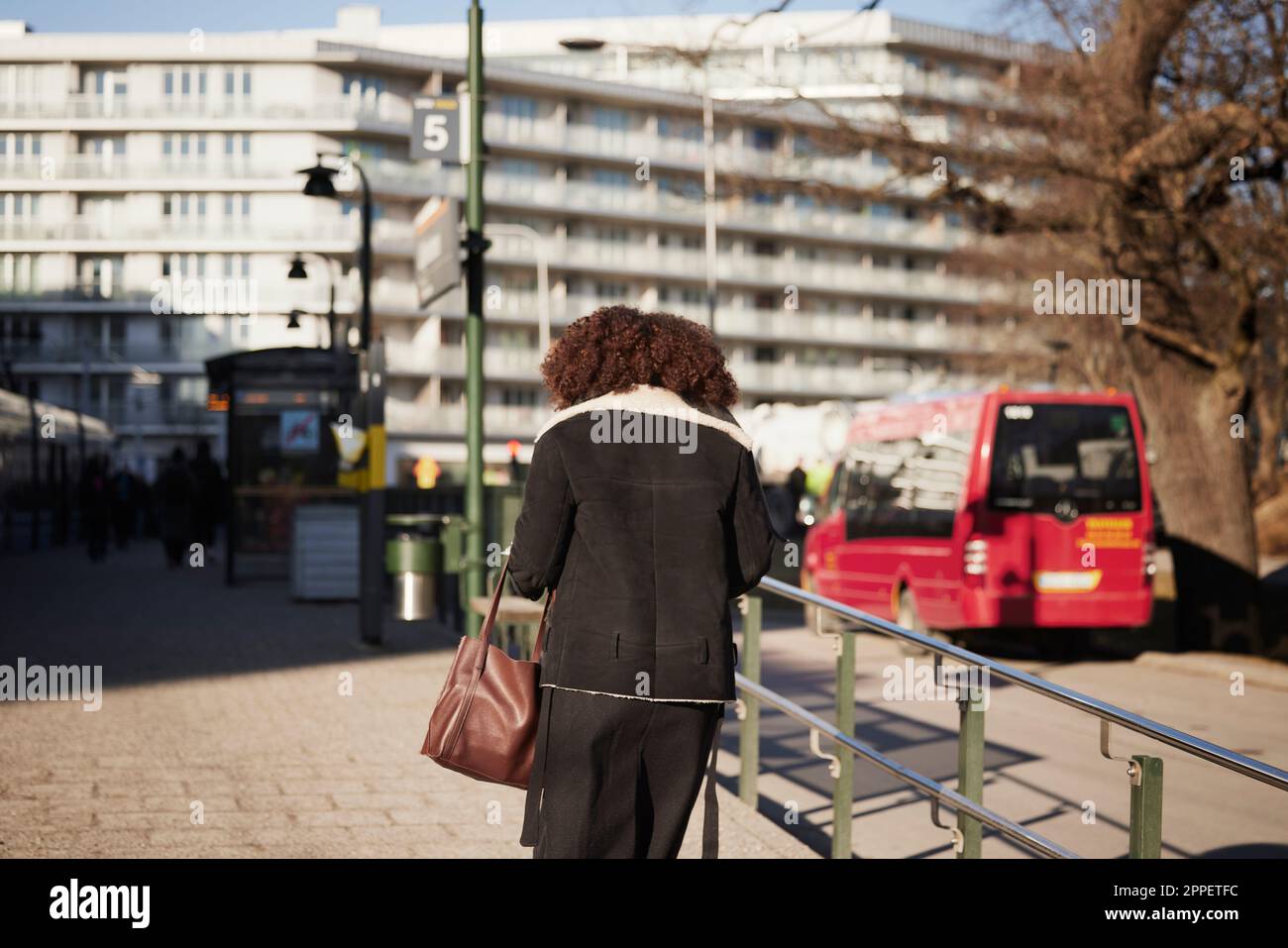 Rear view of woman walking towards bus stop Stock Photo - Alamy