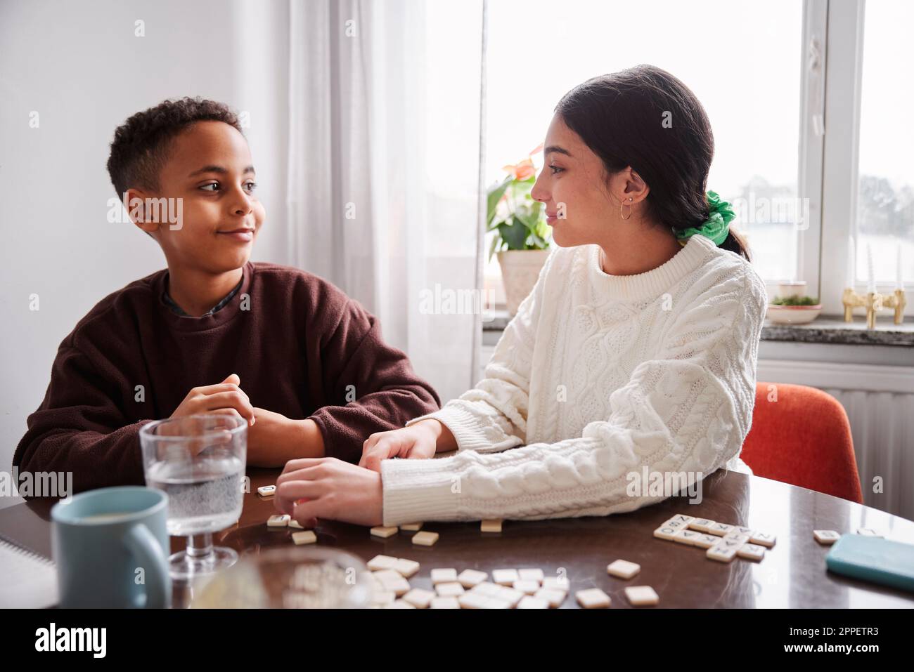 Girl and boy playing scrabble at dining table Stock Photo - Alamy