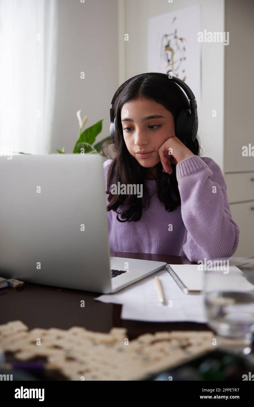 Girl doing homework with laptop at dining table Stock Photo - Alamy