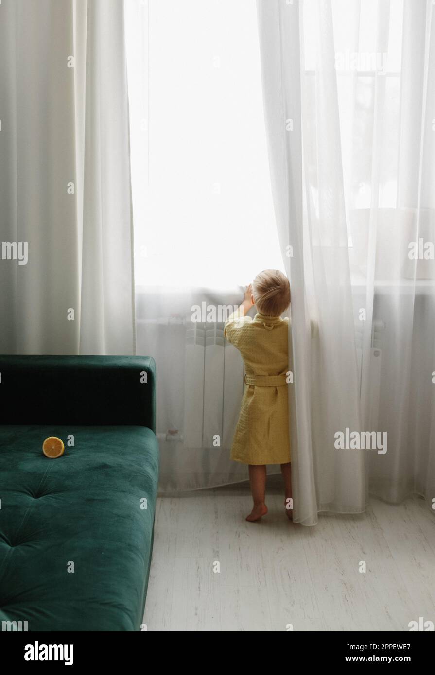 A little boy in a dressing gown stands near the window and looks Stock ...