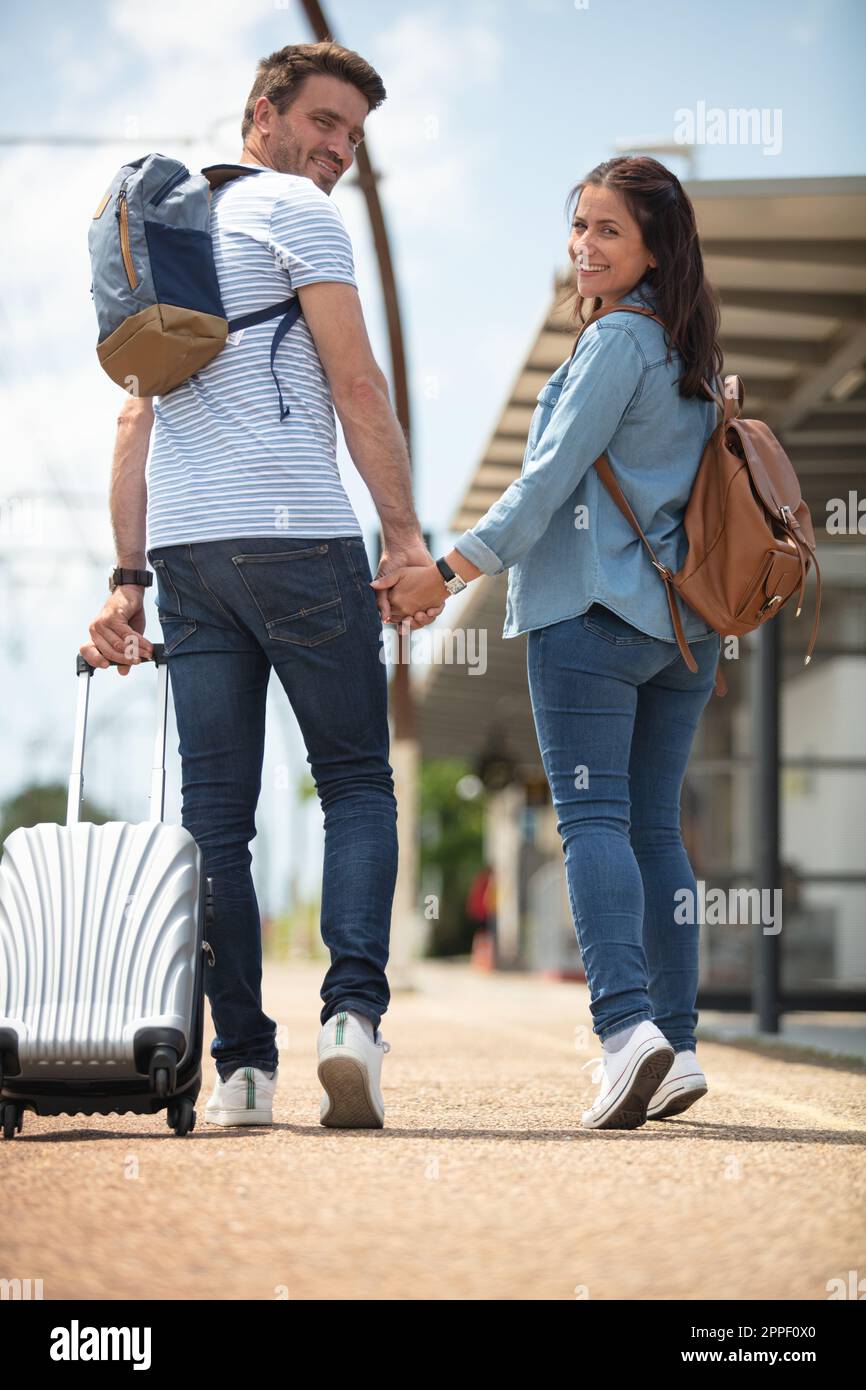 couple walking holding hands and pulling a suitcase Stock Photo - Alamy