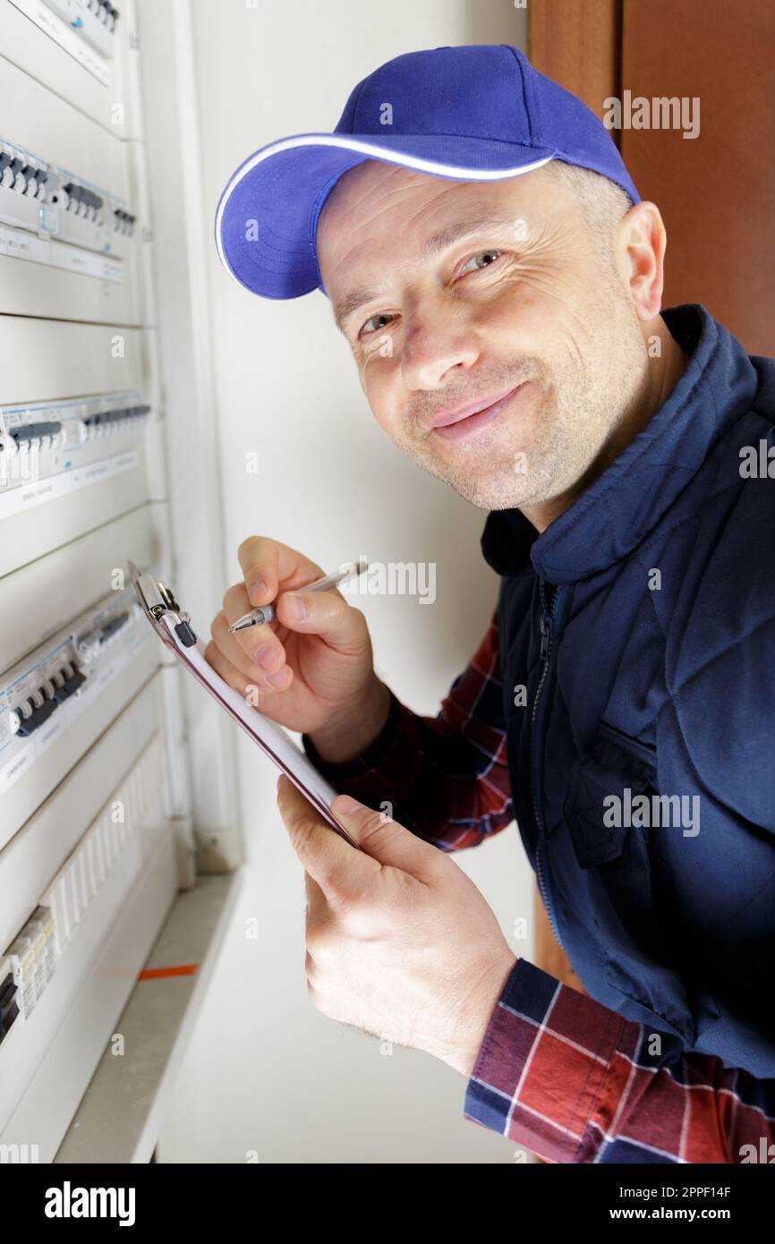 male technician writing on clipboard in front of fuse box Stock Photo ...