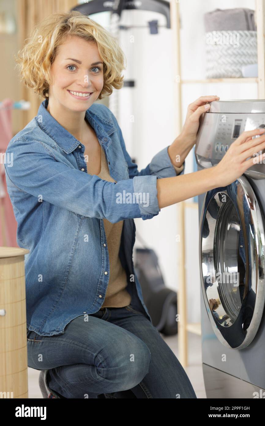 woman smiling at camera while putting laundry into washing machine ...