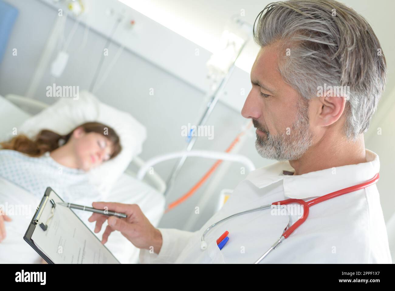 doctor reading notes of young woman in hospital bed Stock Photo - Alamy