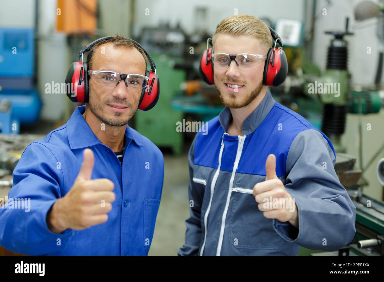 portrait of two engineers in machinery workshop holding thumbs up Stock ...