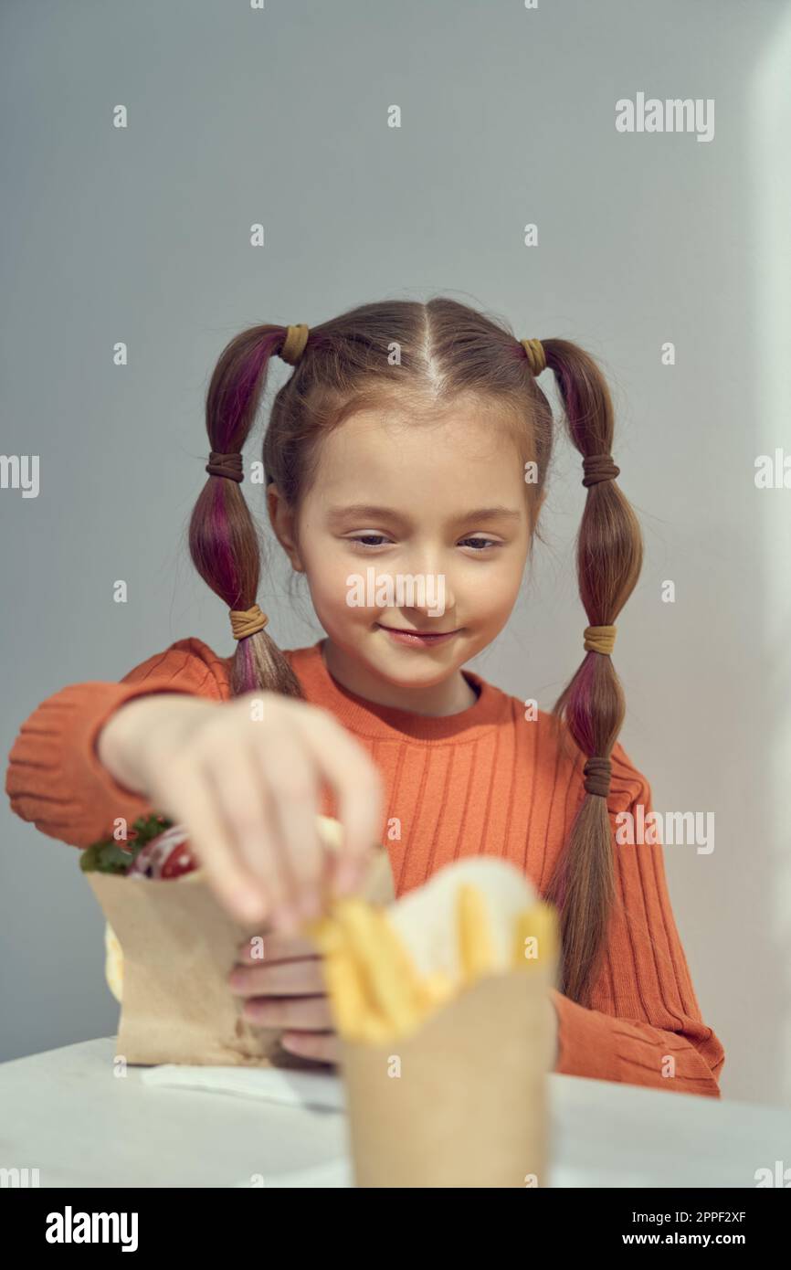 Cheerful little girl eating fries. Portrait of a beautiful white child ...