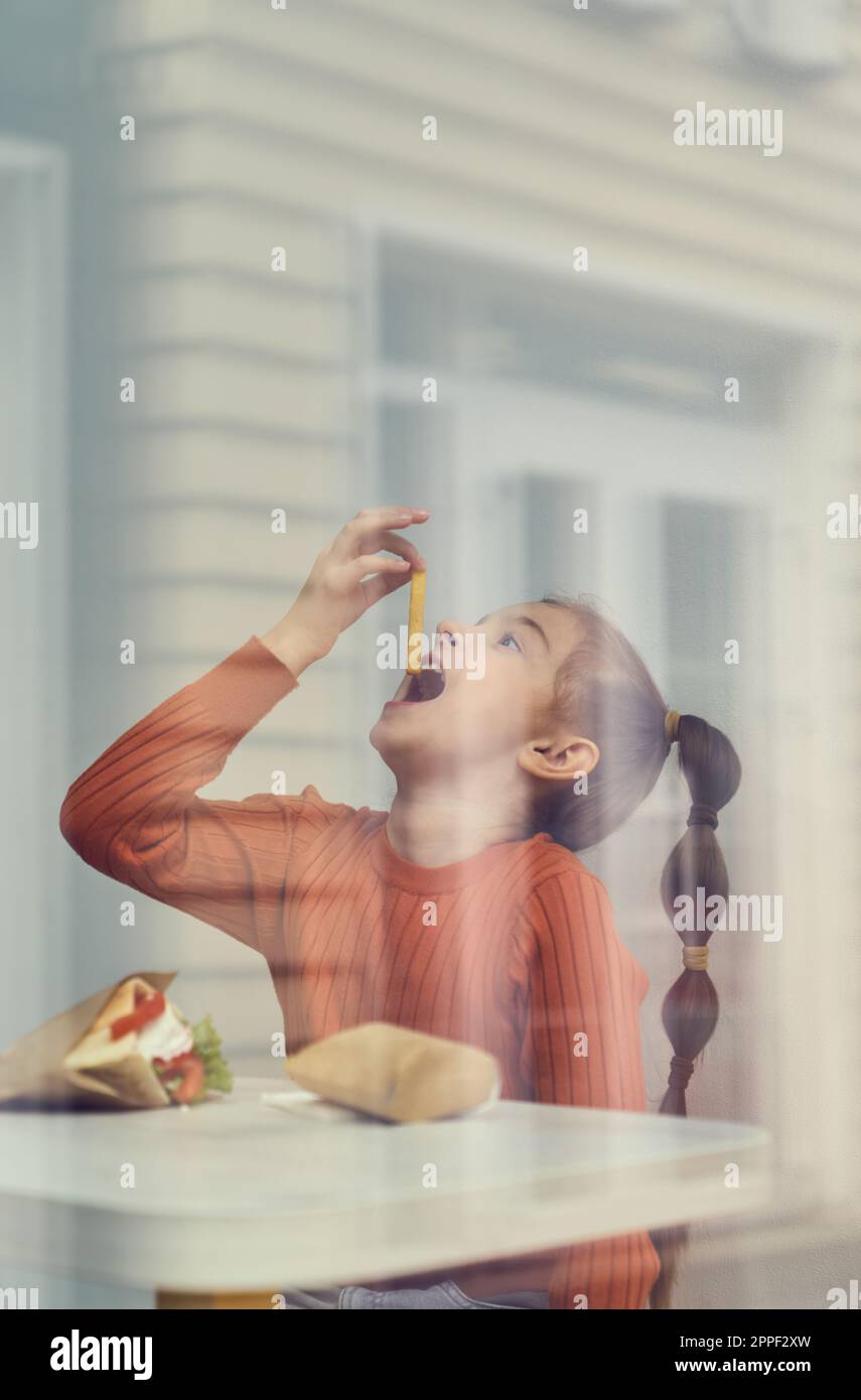 Hungry little girl eating fries in a fast food restaurant. Cute white ...