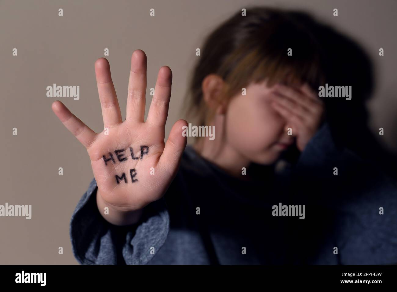 Crying little girl showing palm with phrase HELP ME near beige wall ...