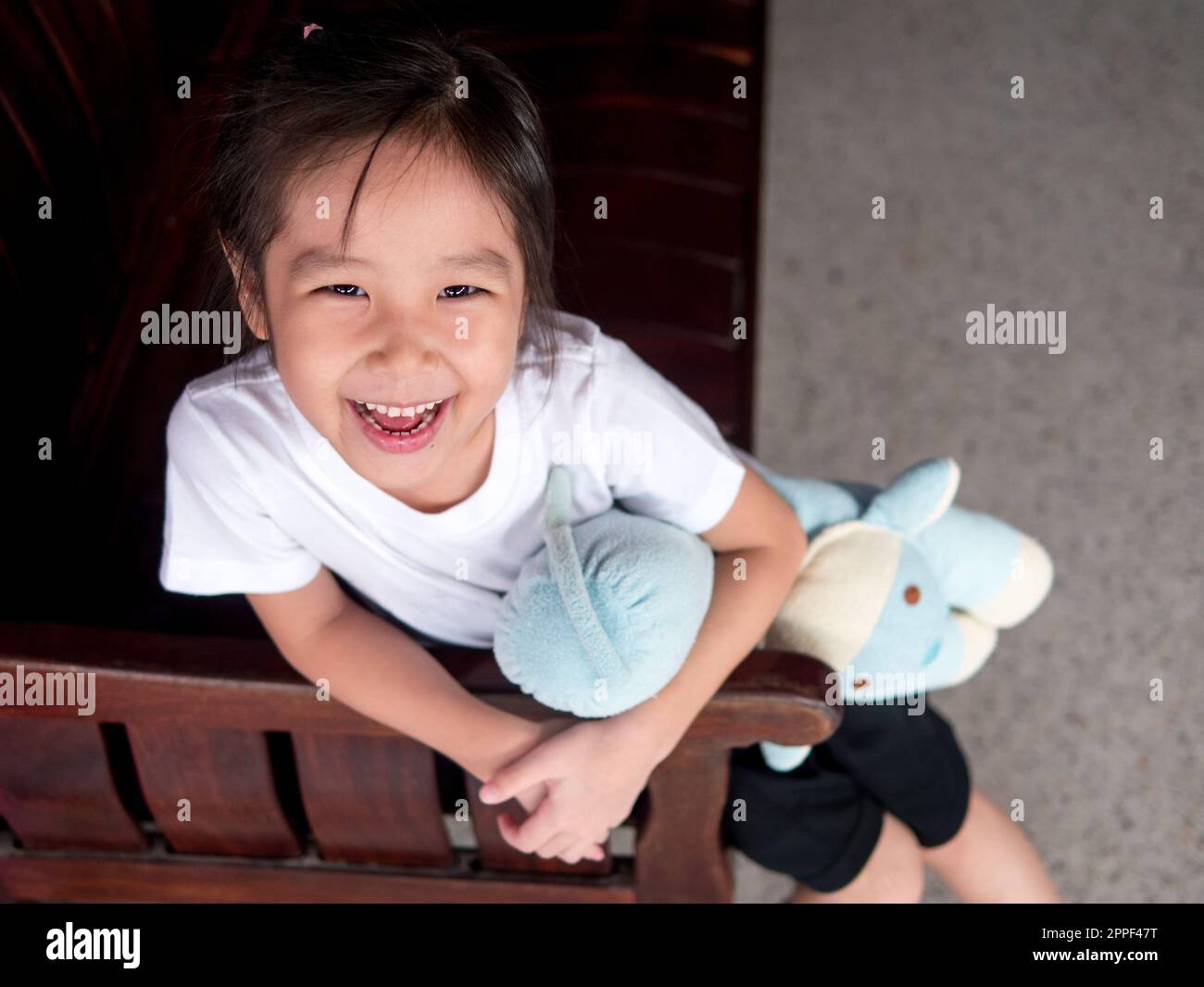 portrait of a little asian kid girl, hug her bolster, smile face , sit down on the wood sofa ...