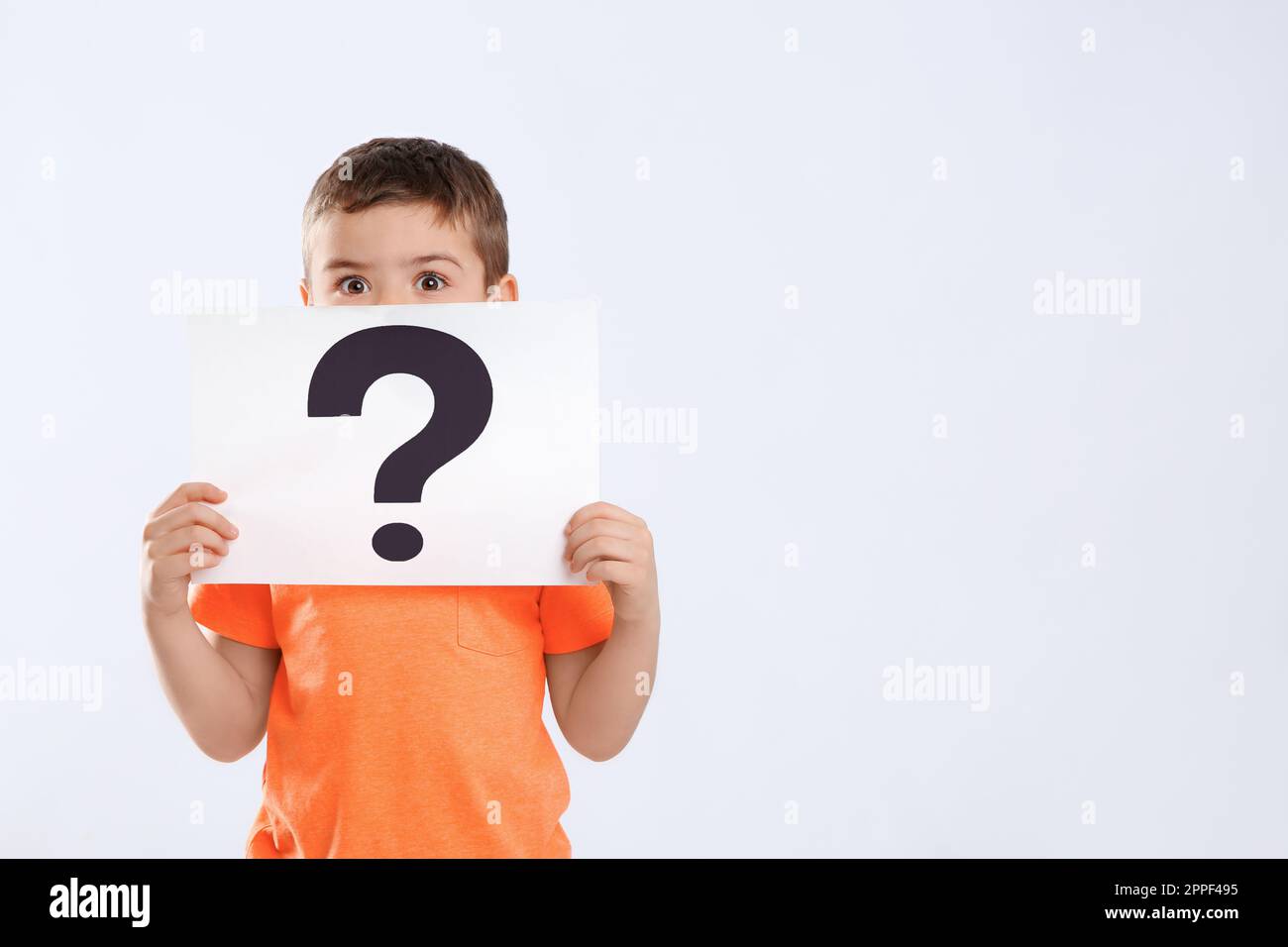Emotional little boy holding paper with question mark on white ...