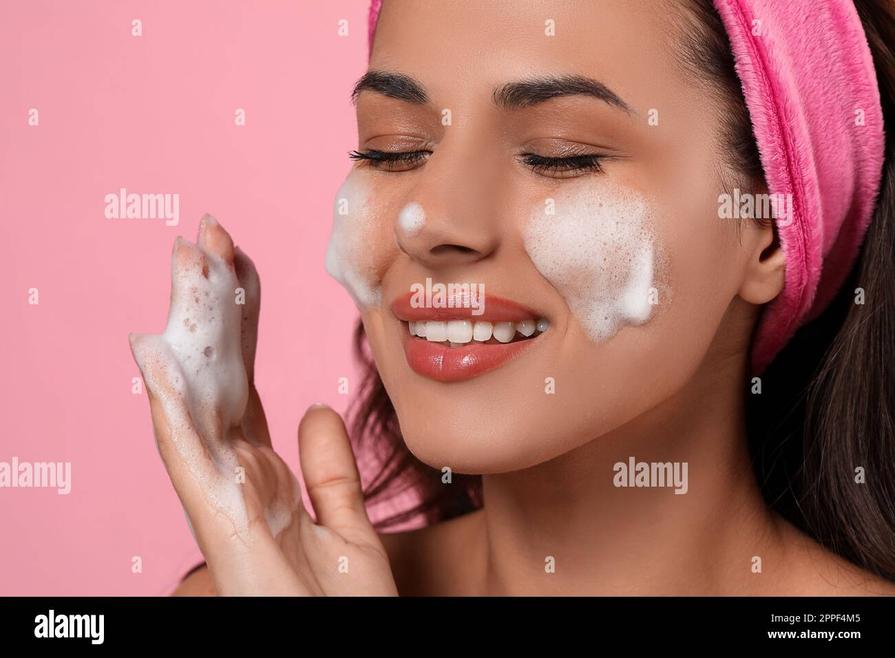 Beautiful Woman Applying Facial Cleansing Foam On Pink Background