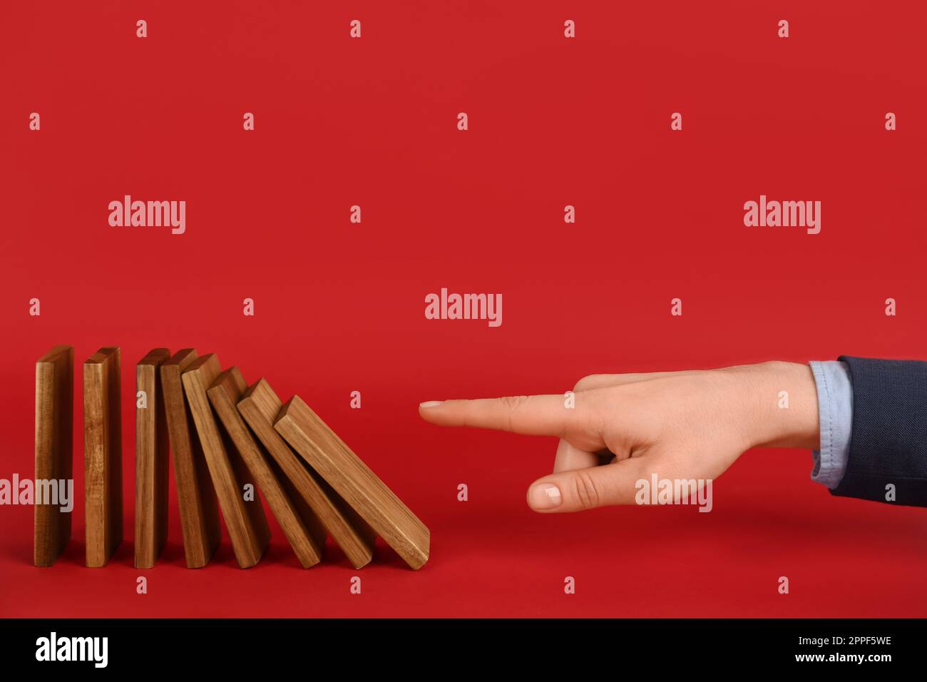 Woman causing chain reaction by pushing domino tile on red background ...