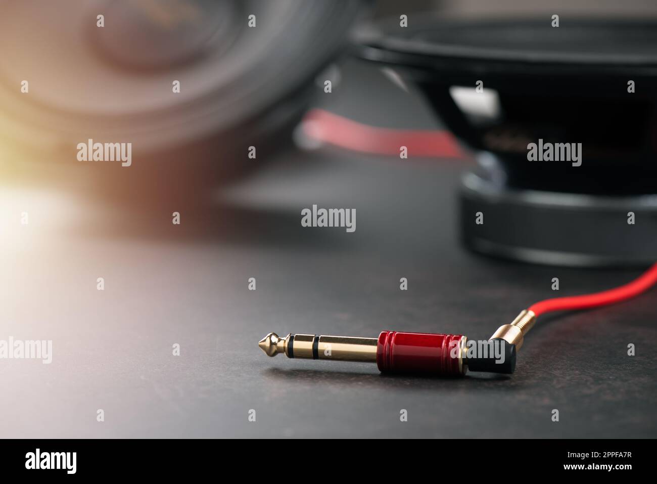 Close up red AUX(Auxiliary) cable with Male jack with speaker in the background. Cable for ...