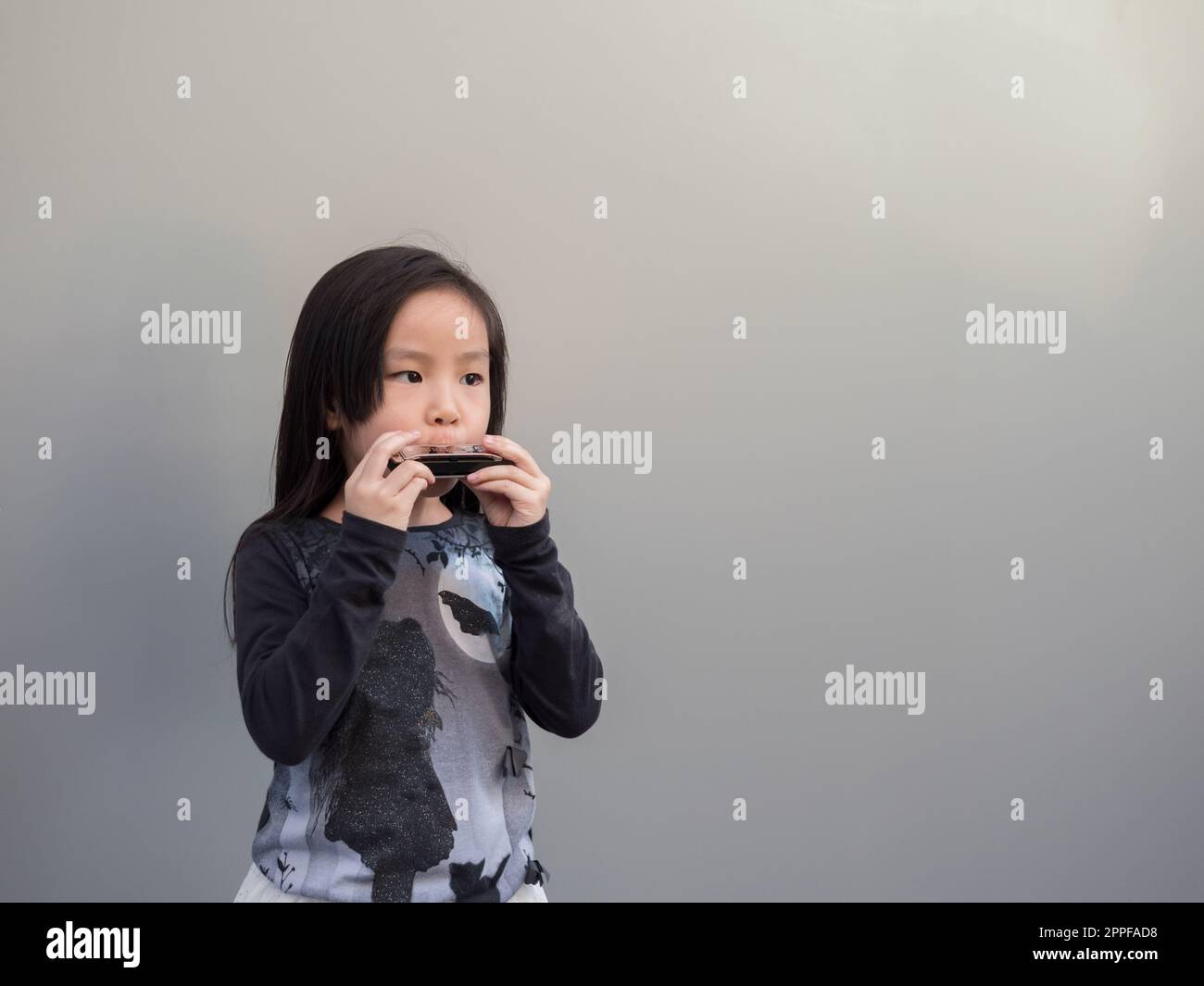 Little asian child play the harmonica, gray background Stock Photo - Alamy