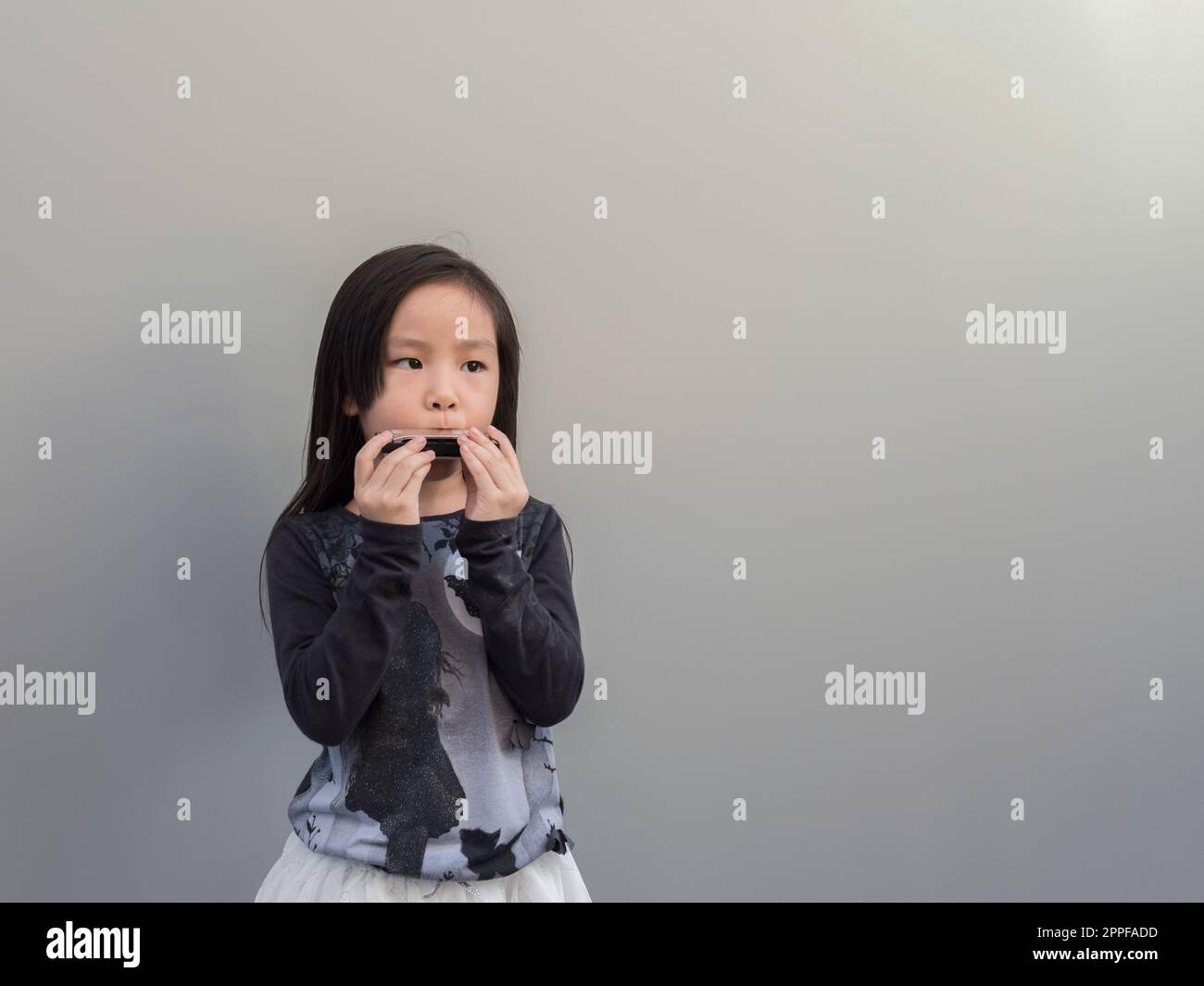 Little asian child play the harmonica, gray background Stock Photo - Alamy