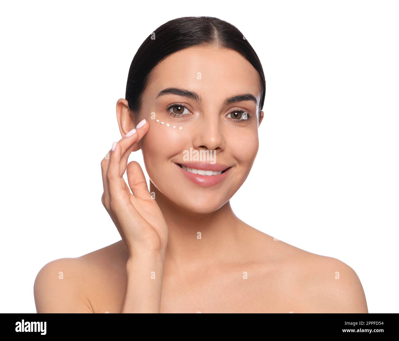 Beautiful young woman with cream on skin under eye against white ...