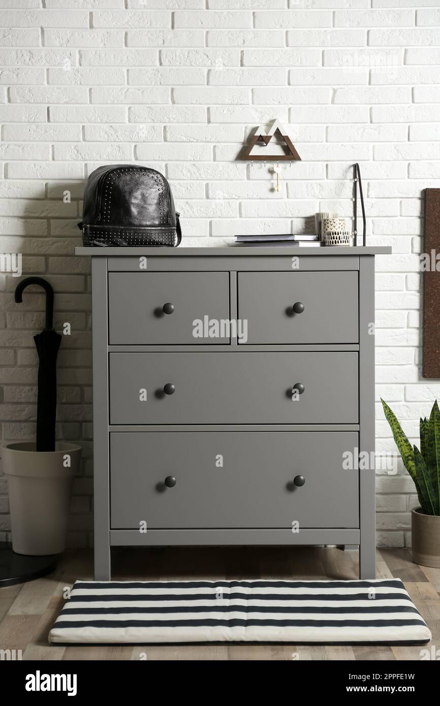 Grey chest of drawers near white brick wall indoors Stock Photo - Alamy