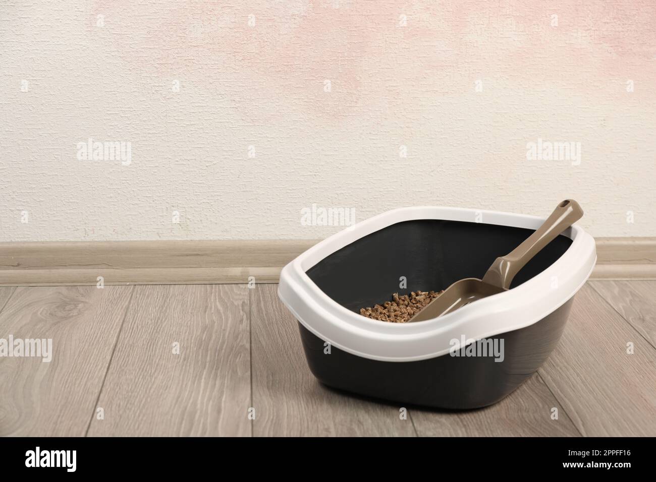 Cat tray with biodegradable litter and scoop on floor near pink wall ...