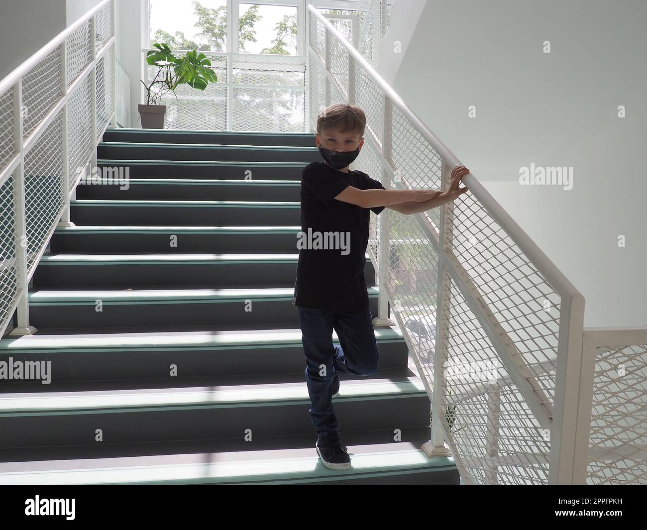 A blond boy 8 years old in black clothes and a mask stands on a white ...