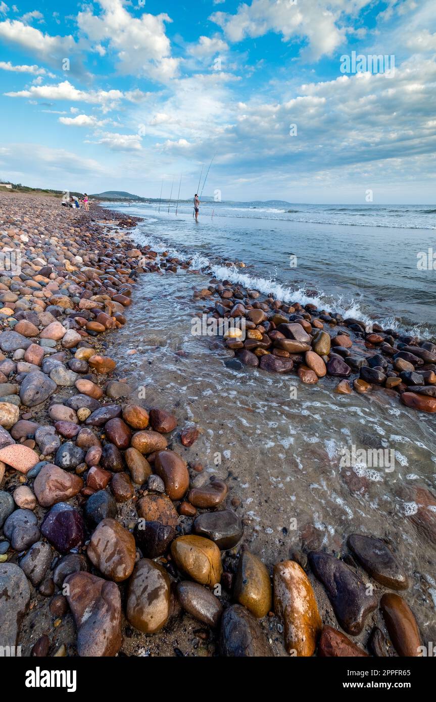 Some fishermen wait next to their fishing poles on a pebble beach Stock ...
