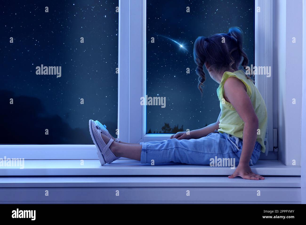 Cute little girl sitting near window and looking at shooting star in ...