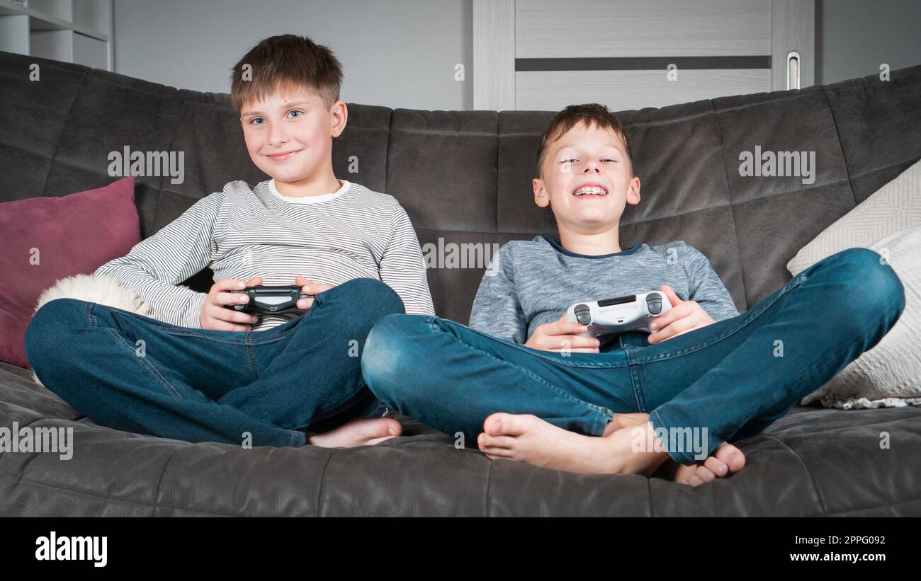 Portrait of two satisfied teenage boys sitting on sofa at home, holding ...