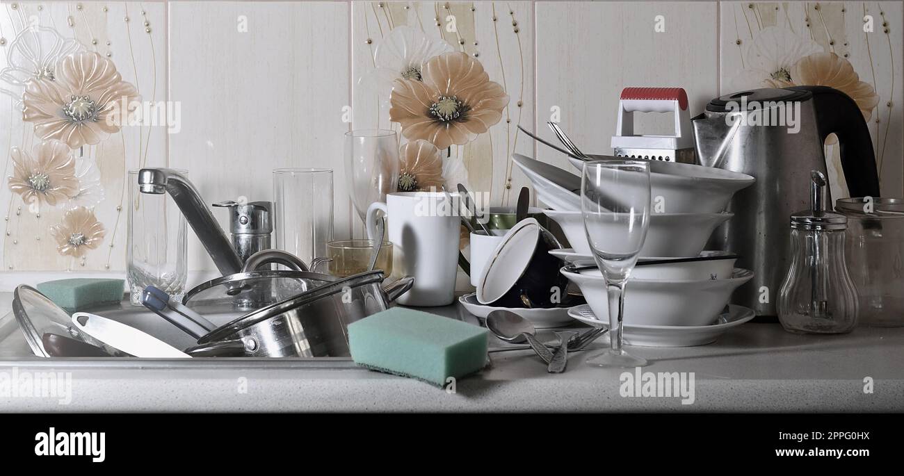 A huge pile of unwashed dishes in the kitchen sink and on the ...